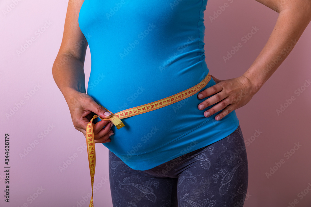 Pregnant female measuring tummy belly with yellow centimeter. Third ...