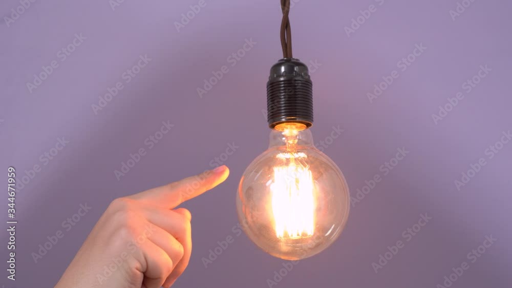 Human hand gently touches luminous bulb hanging on wire with finger ...