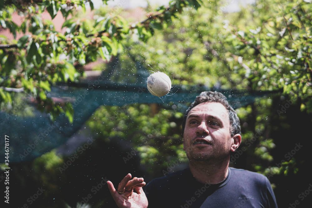 Man in his forties throws and spins a ball that makes water spirals on ...