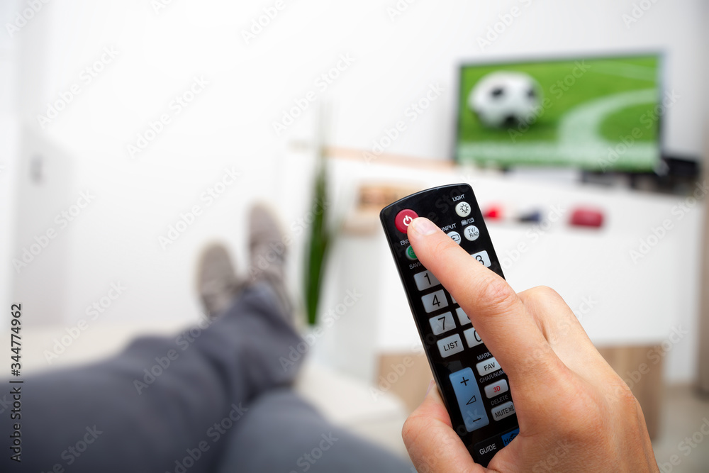 Turning off the TV. Remote control in hand. Man lying watching football ...