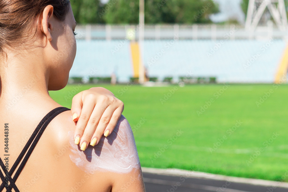 Fitness woman is applying sunscreen on her shoulder before training at ...
