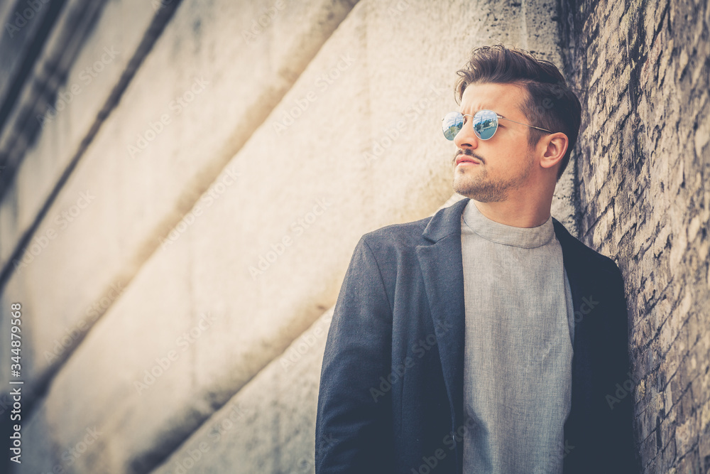 Handsome stylish man leaning on a wall with sunglasses and modern ...