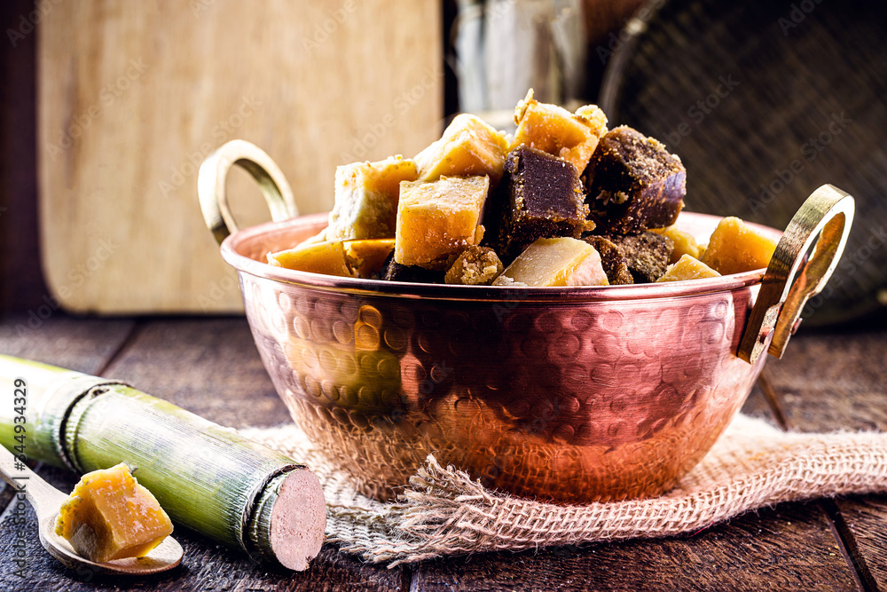Candy in a copper pot on a rustic table. Rapadura is a sugar cane-based ...