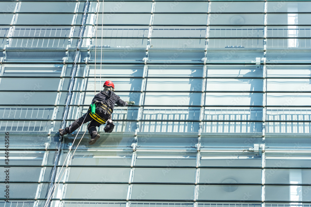 Window cleaner with safety equipment on the shiny glass facade of a ...