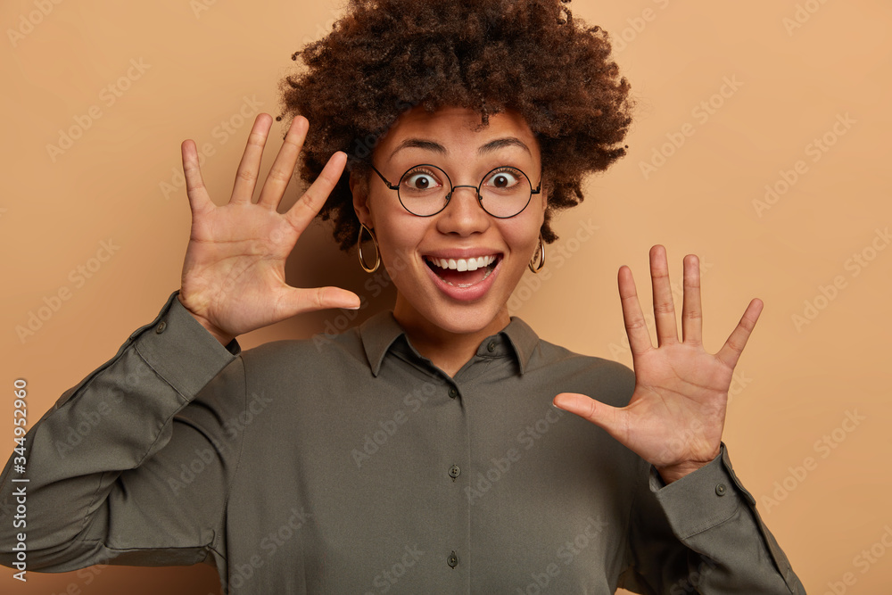 Joyful ethnic woman shows hands up, gestures ten, raises palms and ...