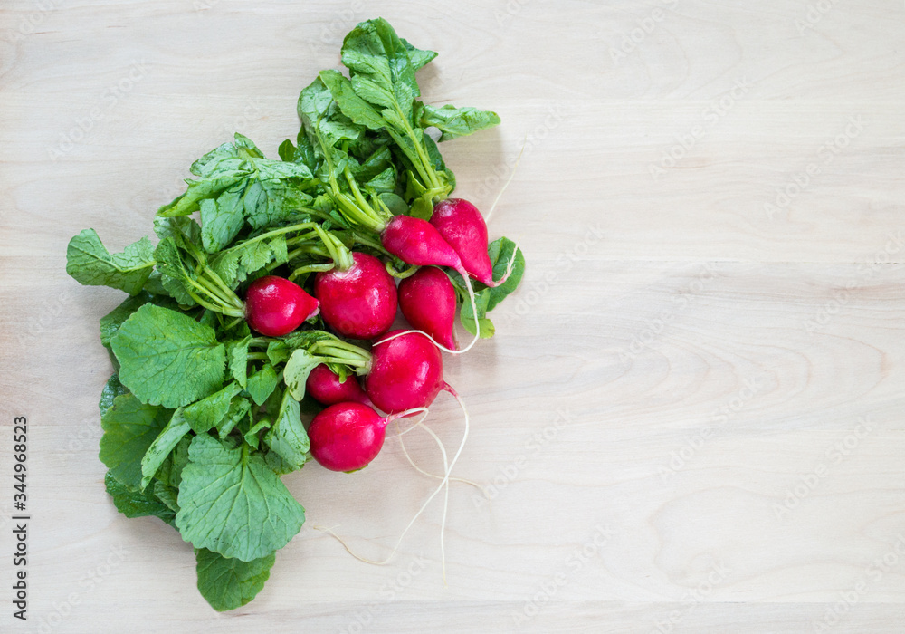 ripe red radishes with leaves and stems on a wood background with copy ...