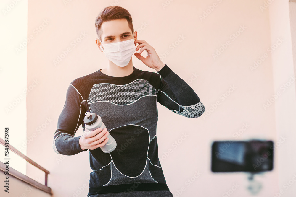 Confident sports man in medical face mask recording video tutorial for ...