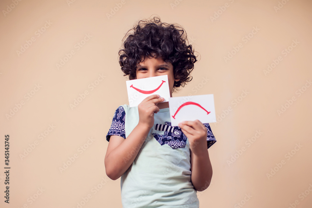 A portrait of kid boy holding cards with positive and negative smile ...