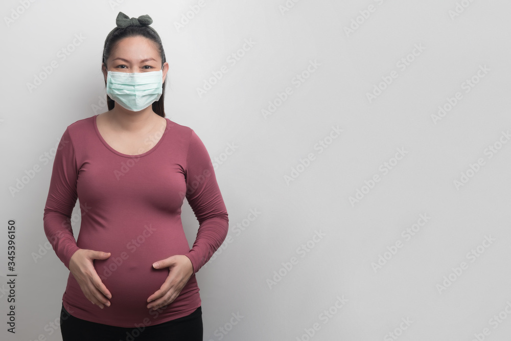 Asian pregnant woman wearing surgical mask looking at camera and ...