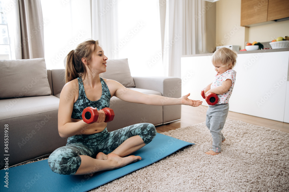 Sports mom. Young mother doing sports with dumbbells at home sitting on ...
