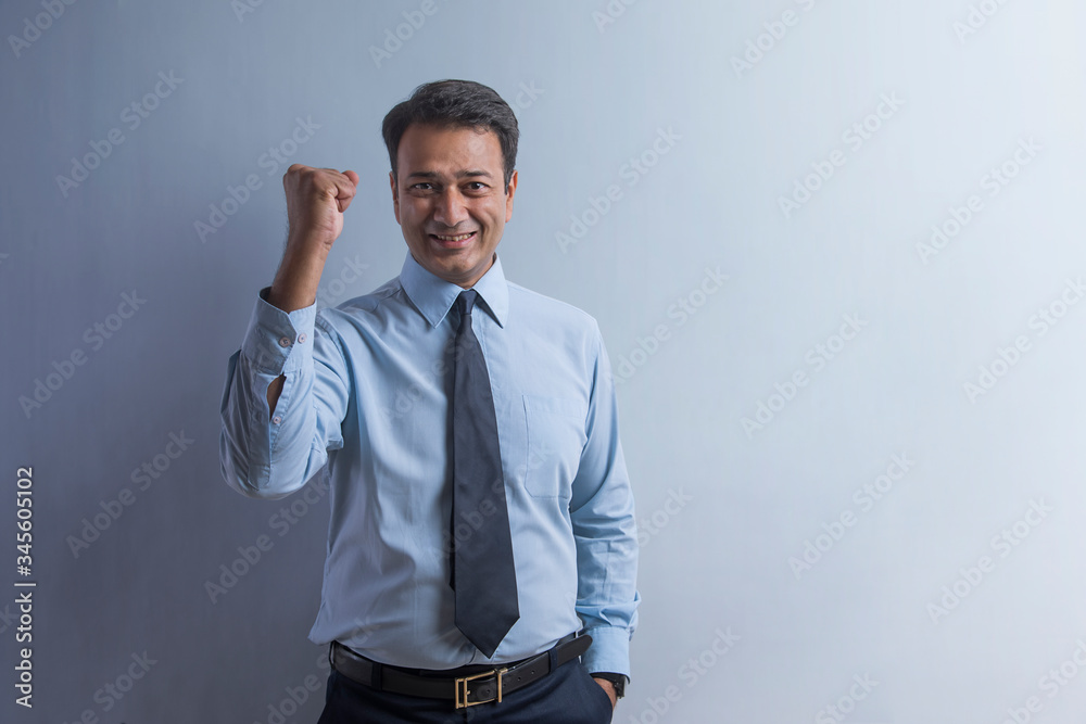Smiling businessman in formal clothes showing raised fist with one hand ...
