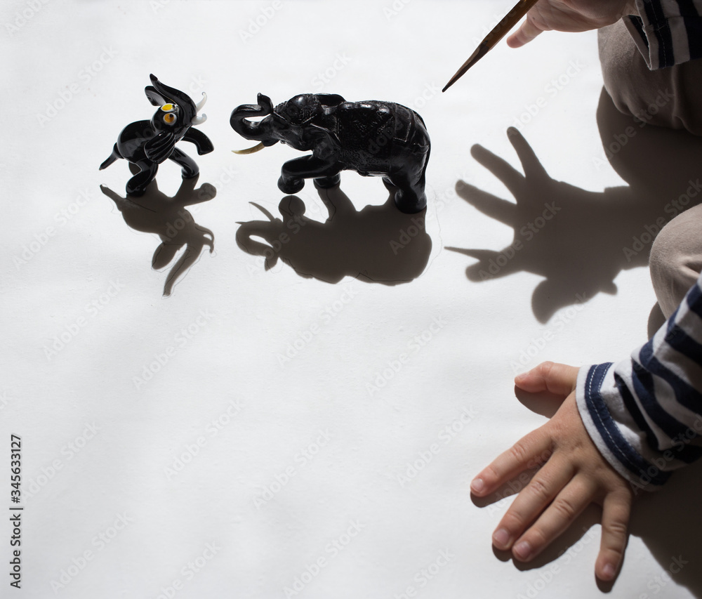 child draws pencil with contrasting shadows from decorative figures of ...