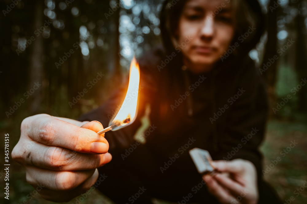Teenage bully in hood holds burning match in his hand. Forest arsonist ...