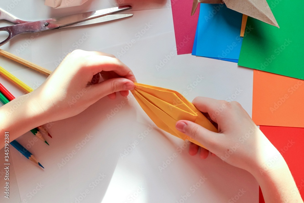 Children’s hands doing origami crane from yellow paper on white ...