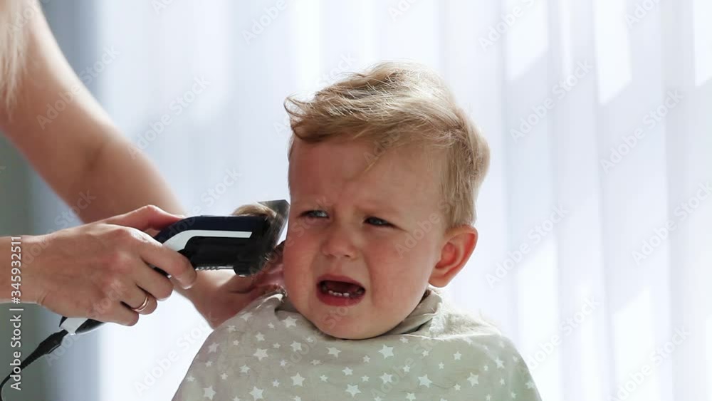 Vidéo Stock Female hands trim a crying baby with an electric hair ...