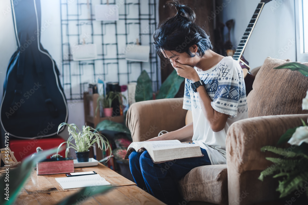 Young man crying when reading story in Bible at home on sofa ...