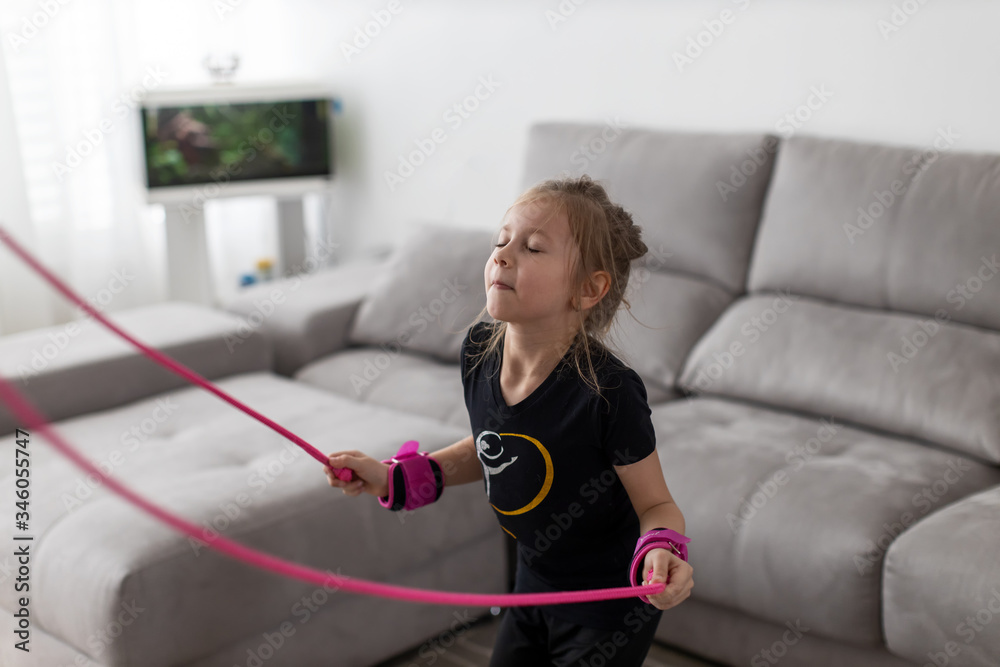 Happy little girl jumping over the rope at home during the isolation ...