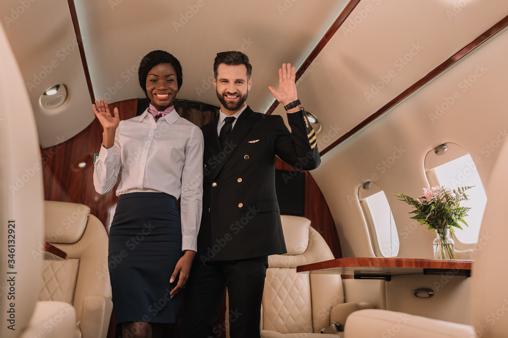 happy pilot and smiling afican american stewardess waving hands while ...