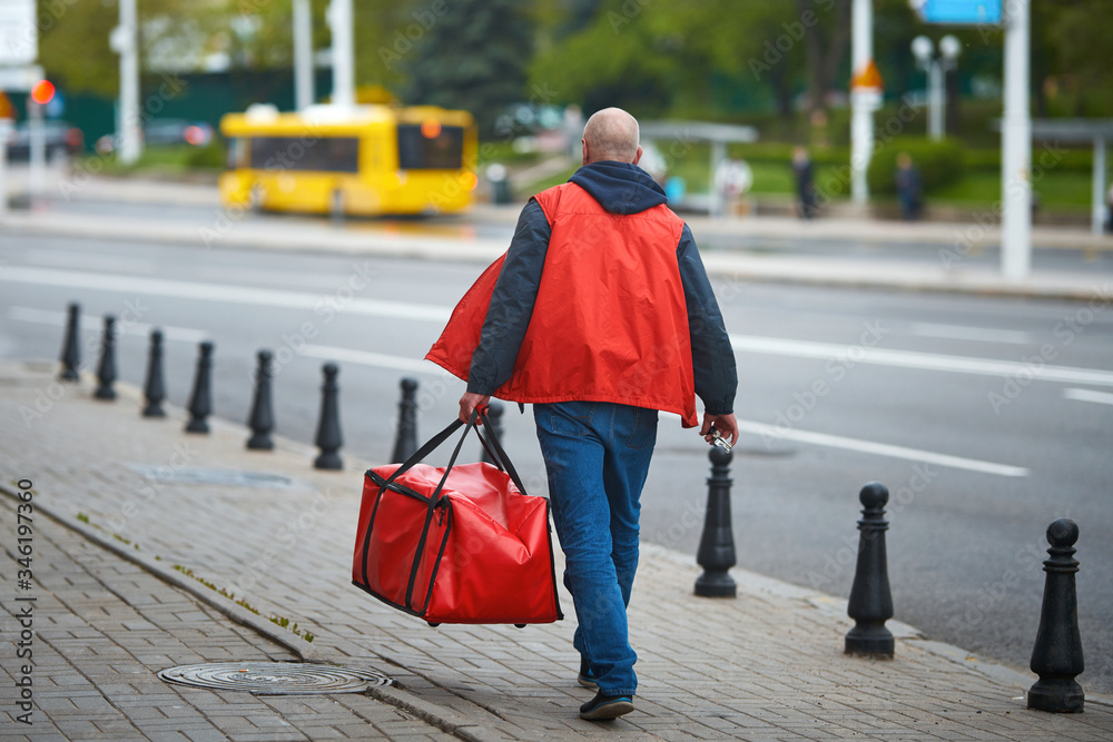Delivery man walking with red thermal bag on city street, food and ...