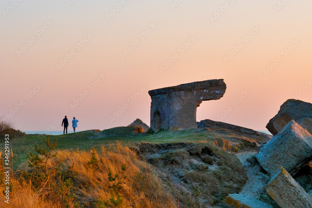 Tourists at sunset visiting the ruins of a sea fort. The sea destroys ...