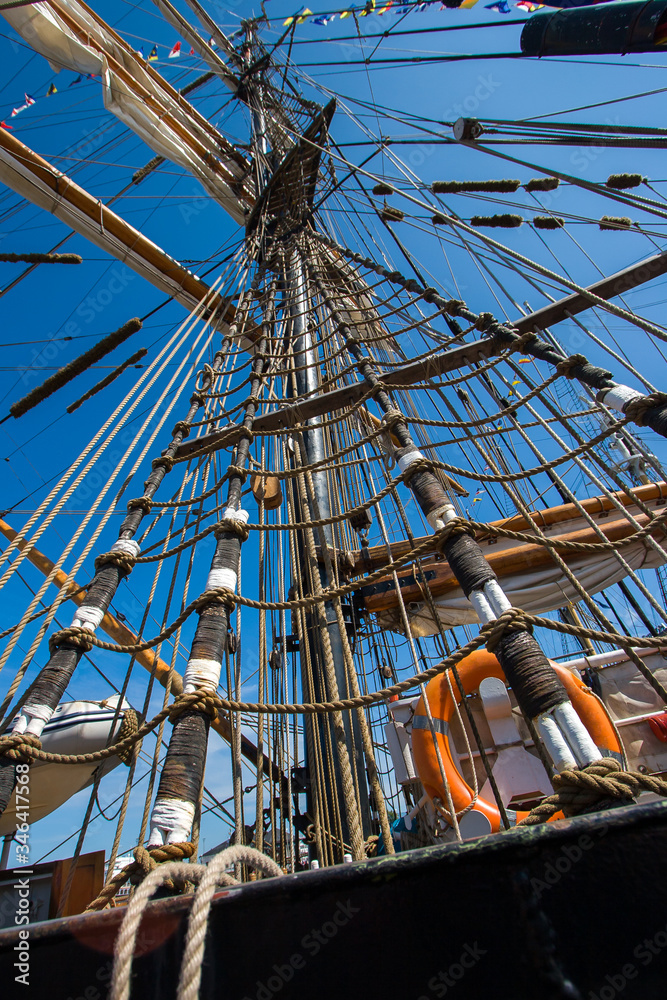 High mast with sails and rope ladders against the blue sky. Lifebuoy ...