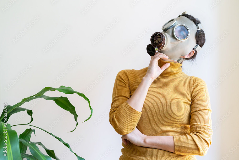 Horizontal view of woman with gas mask surrounded with plants at home ...