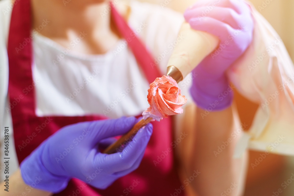 The pastry chef makes a rose flower out of buttercream to decorate the ...