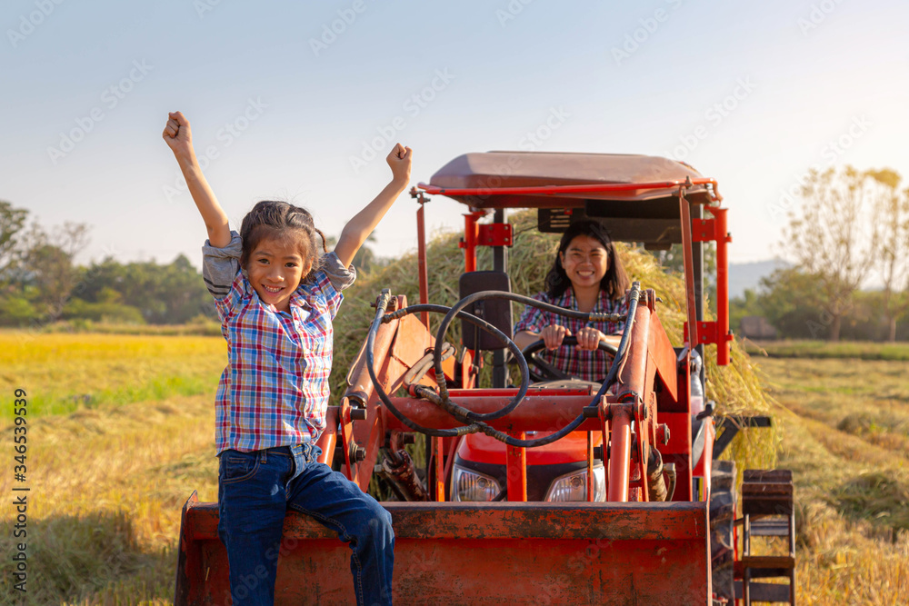 Happy Asian girl sitting on front of tractor with her mother driving a ...