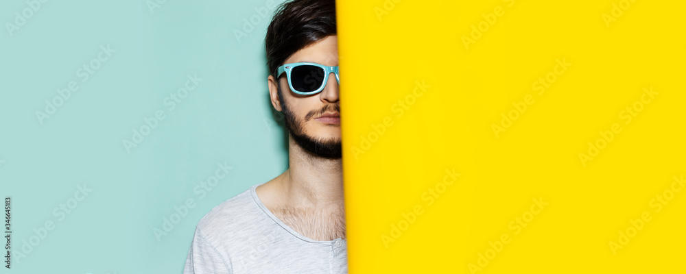 Studio portrait of young confident guy with cyan shades, standing ...