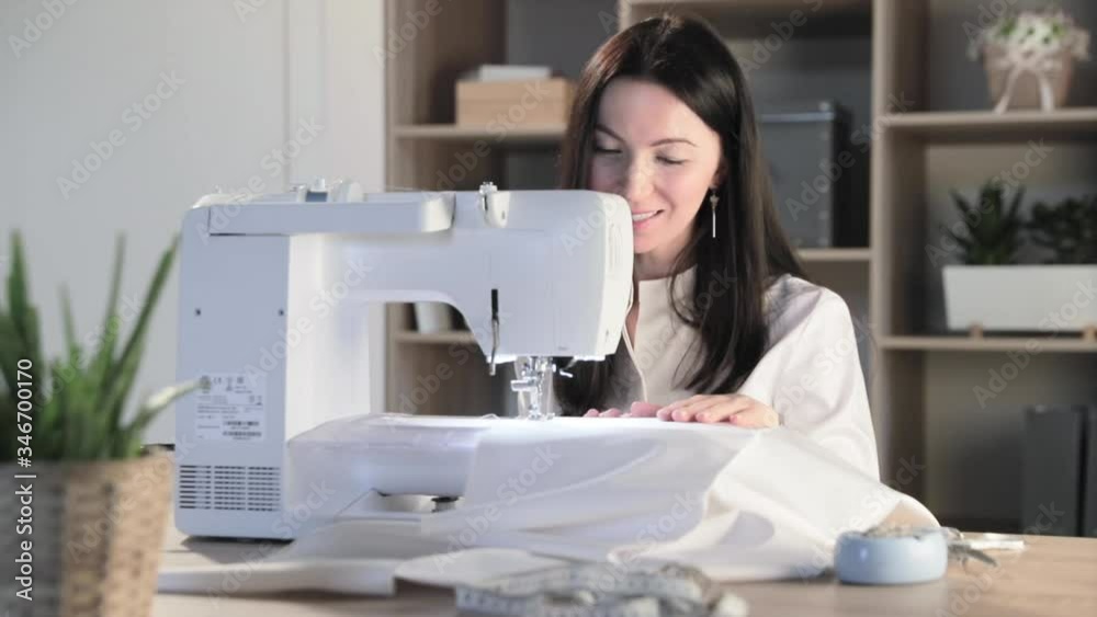 The beautiful young girl sits at the automatic sewing machine in sewing ...