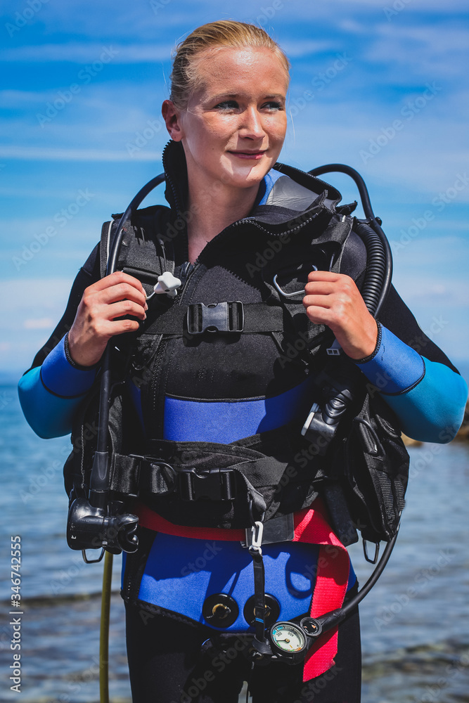 A young female diver, in full gear to go underwater diving. Cute blonde ...