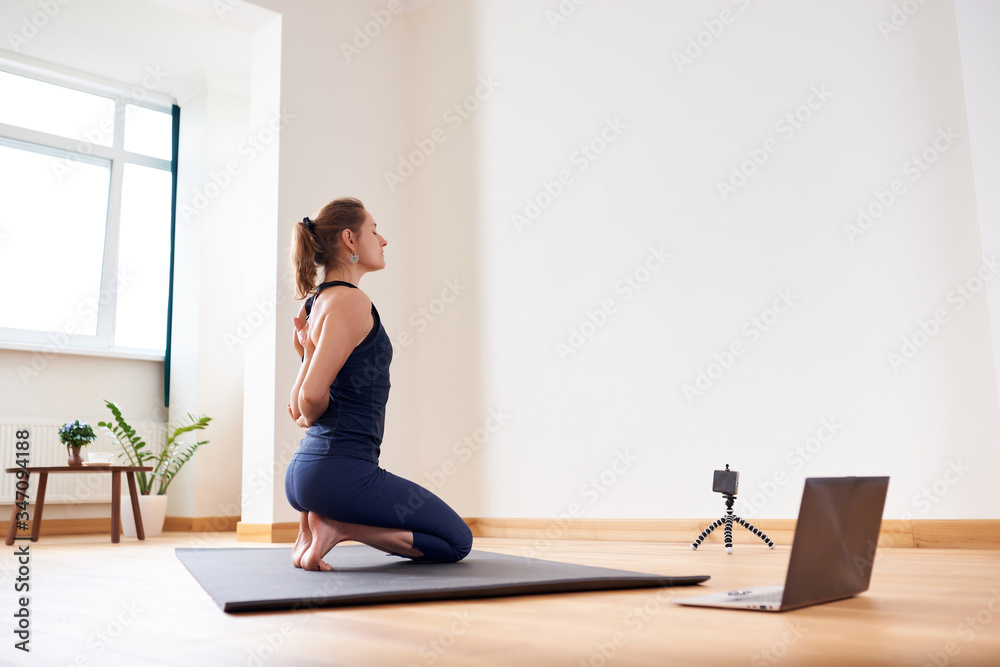 Woman doing yoga online. Computer and camera in her living room ...