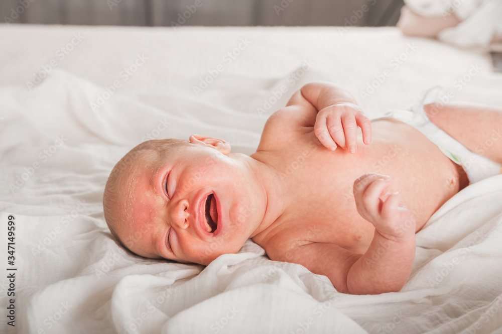 Newborn on the bed. Crying, screaming baby close up and copy space ...