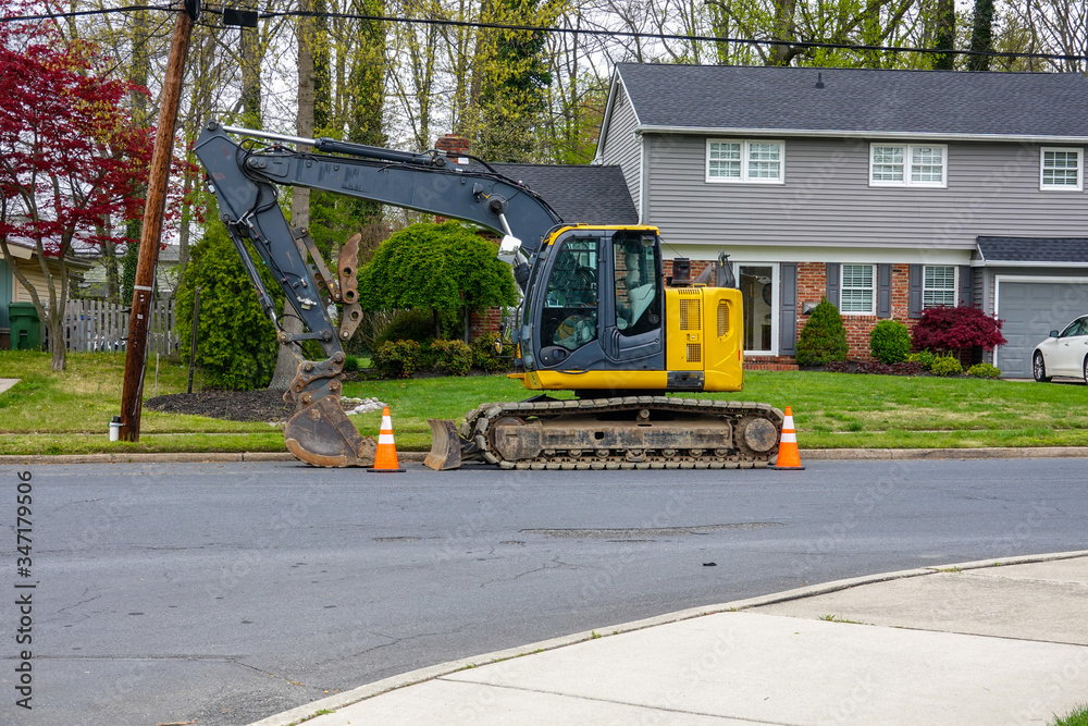 Yellow heavy equipment excavator parked on the side of a residential ...