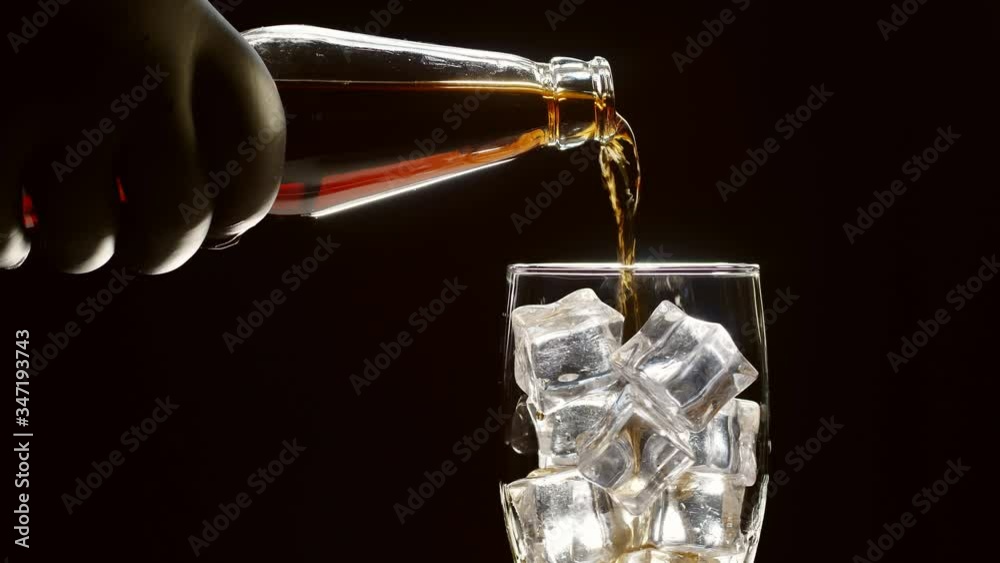 Pouring carbonated drink into a rotating glass with ice cubes close-up. bartender's hand pours ...