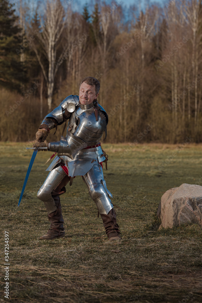 A walking knight in armor and holding a sword in his hands shows combat ...