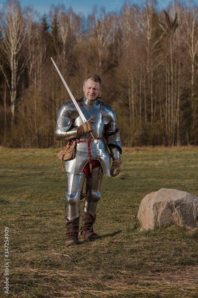A walking knight in armor and holding a sword in his hands shows combat ...