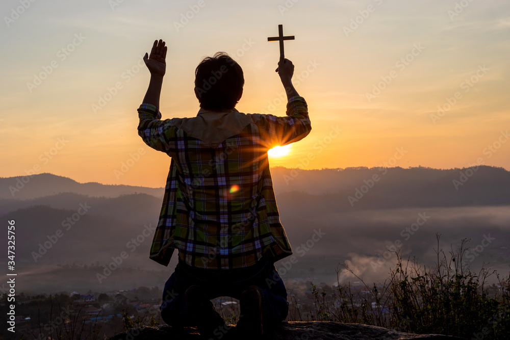 Silhouette of human kneeling down praying and holding christian cross ...