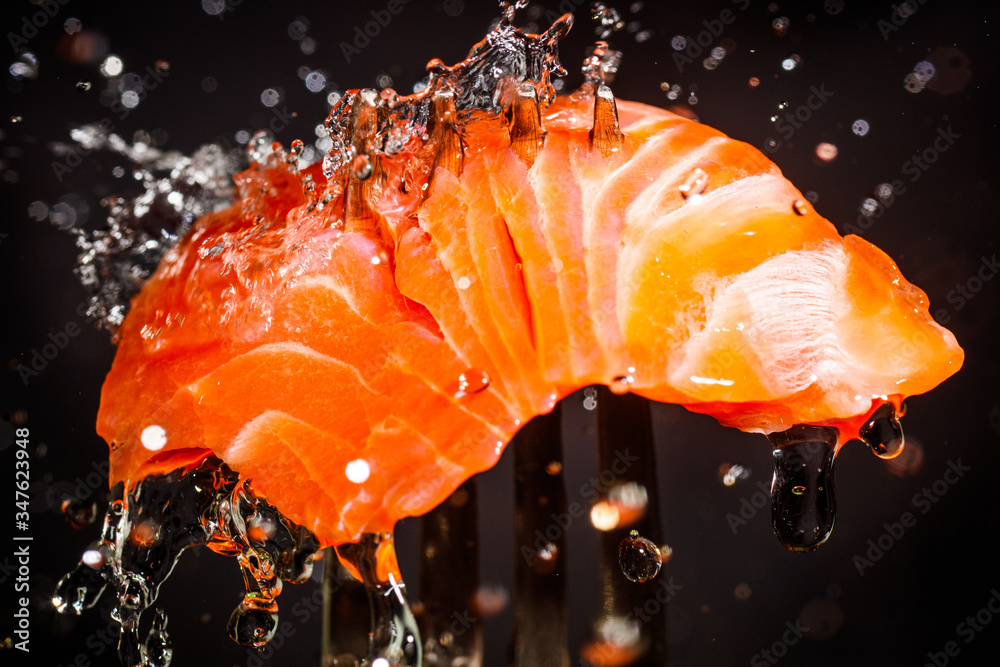 Red fish impaled on a fork in a spray of water on a black background ...