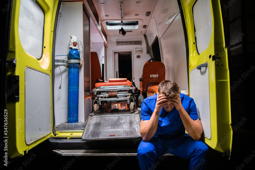 Confused paramedic in a blue uniform sitting in the back of an ...