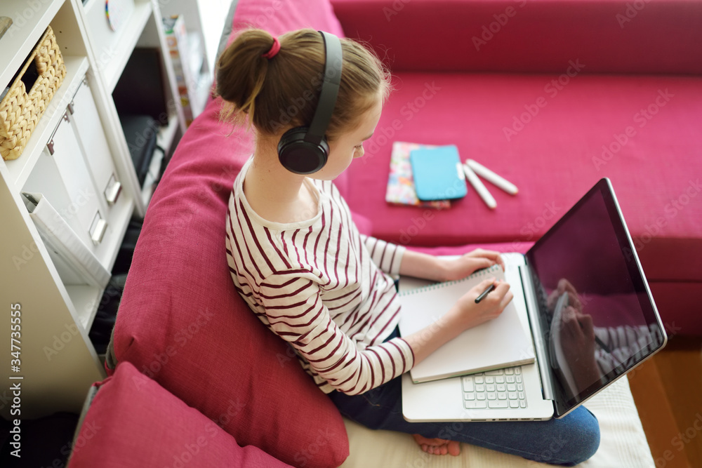 Preteen schoolgirl doing her homework with laptop computer at home ...