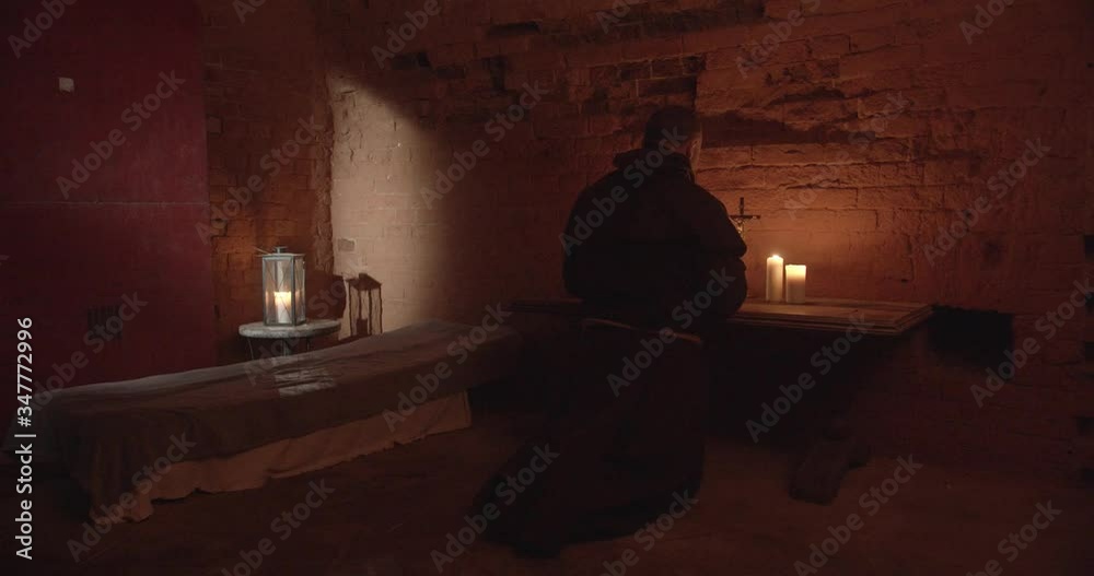 Monk gets on knees, starts praying in front of altar in dark room ...