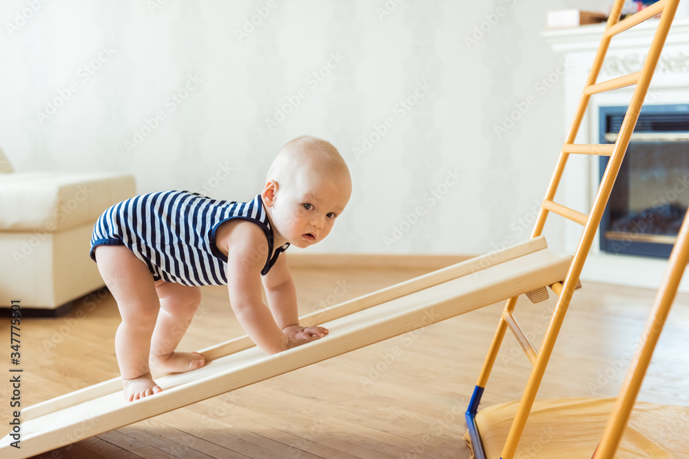 Cute baby performs gymnastic exercises on a wooden home sports complex ...