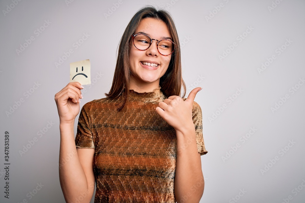 Young beautiful girl holding reminder with sad emotion emoji face over ...