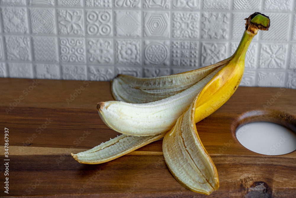 Side view of a yellow banana with peeled off skin which is laying on a ...