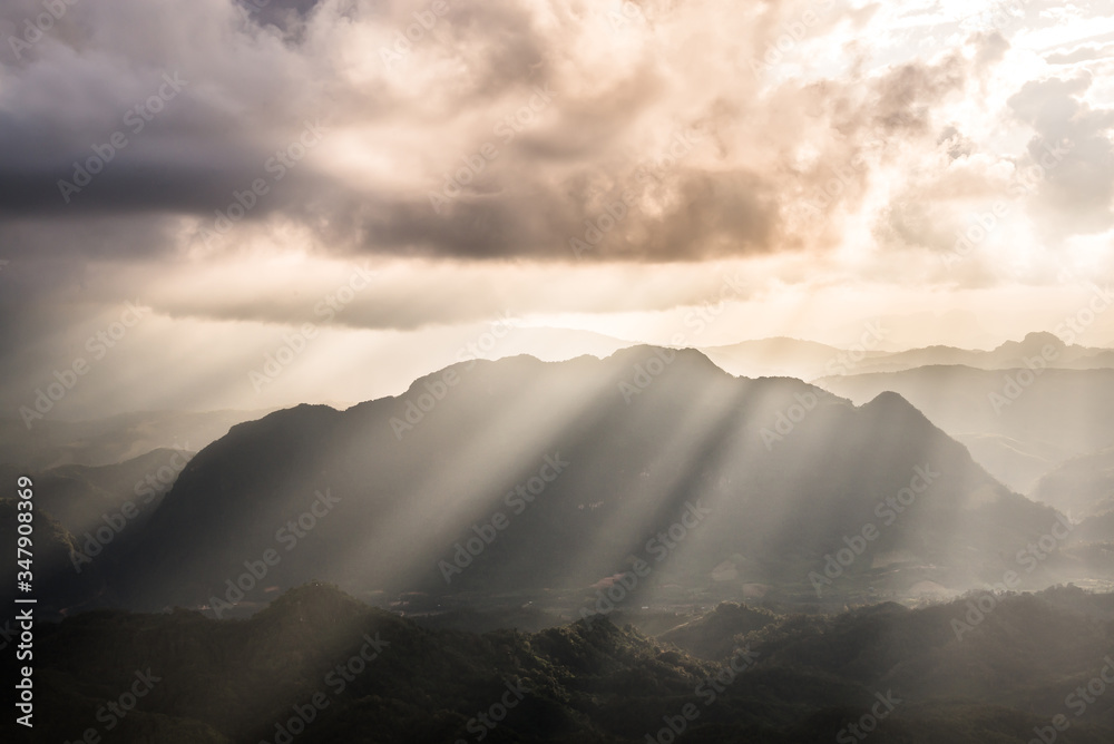 Golden light rays from clouds shining down to mountains. Sun rays over ...