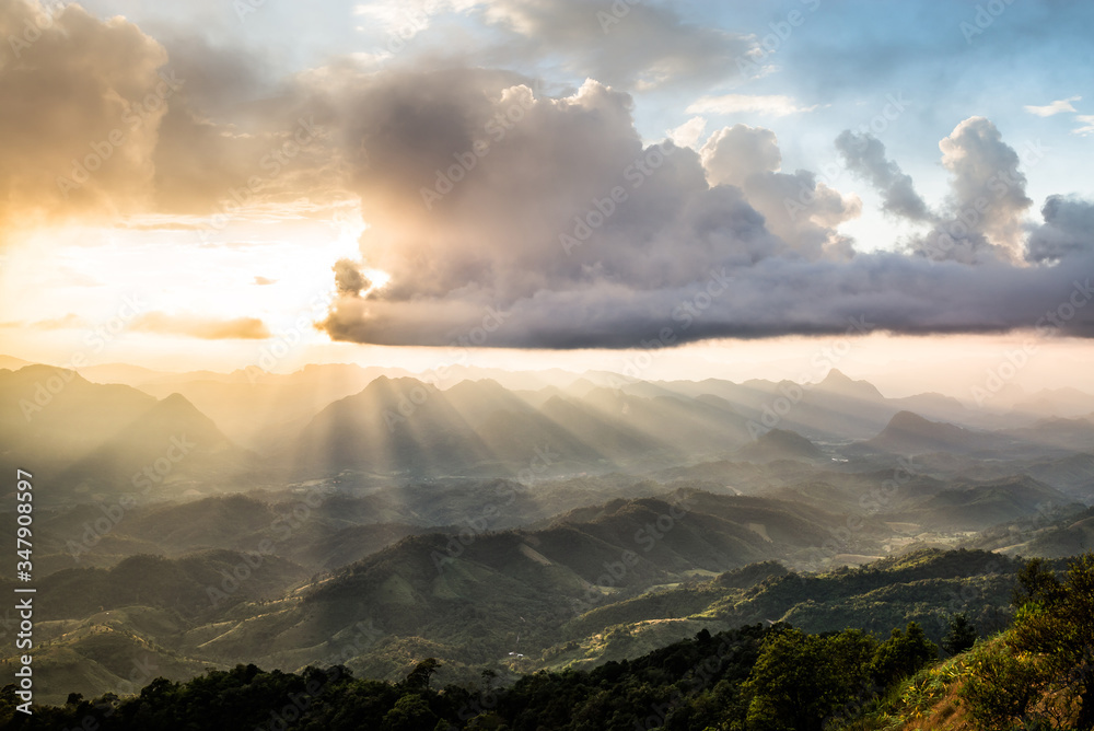 Golden light rays from clouds shining down to mountains. Sun rays over ...