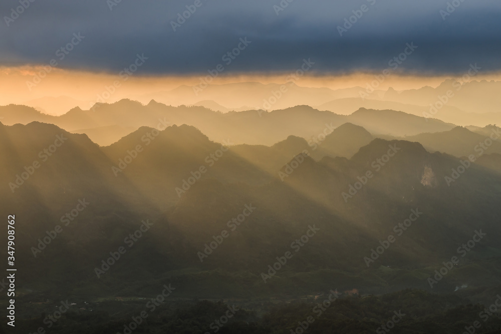 Golden light rays from clouds shining down to mountains. Sun rays over ...