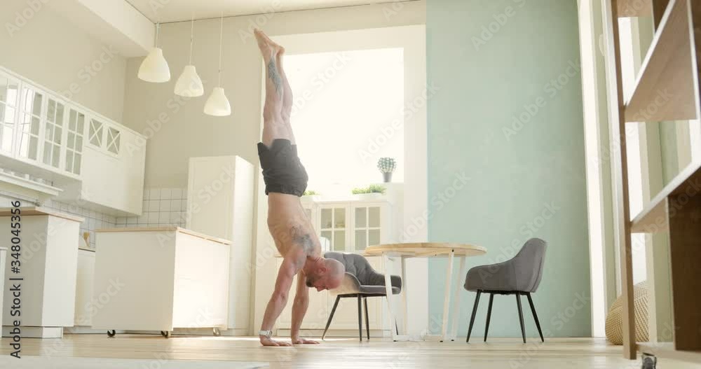 Athletic muscular young man in shorts practicing handstand in kitchen ...