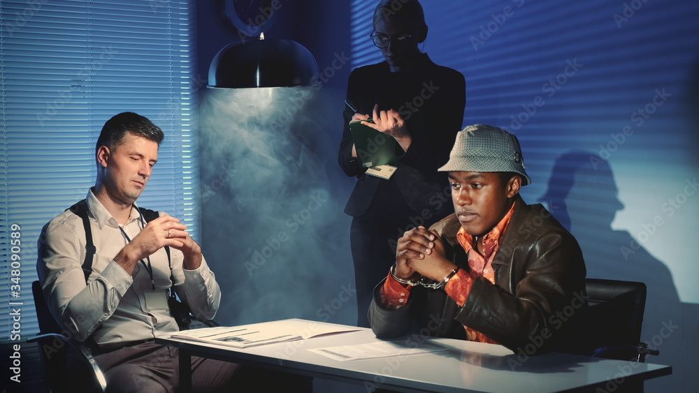 Medium shot of Black prisoner in handcuffs having interview with ...